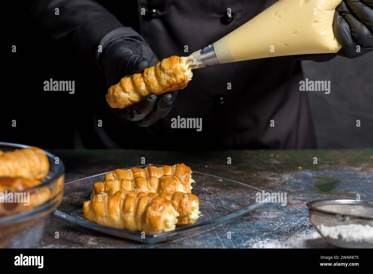 The pastry chef fills puff pastry tubes with custard from a pastry bag ...