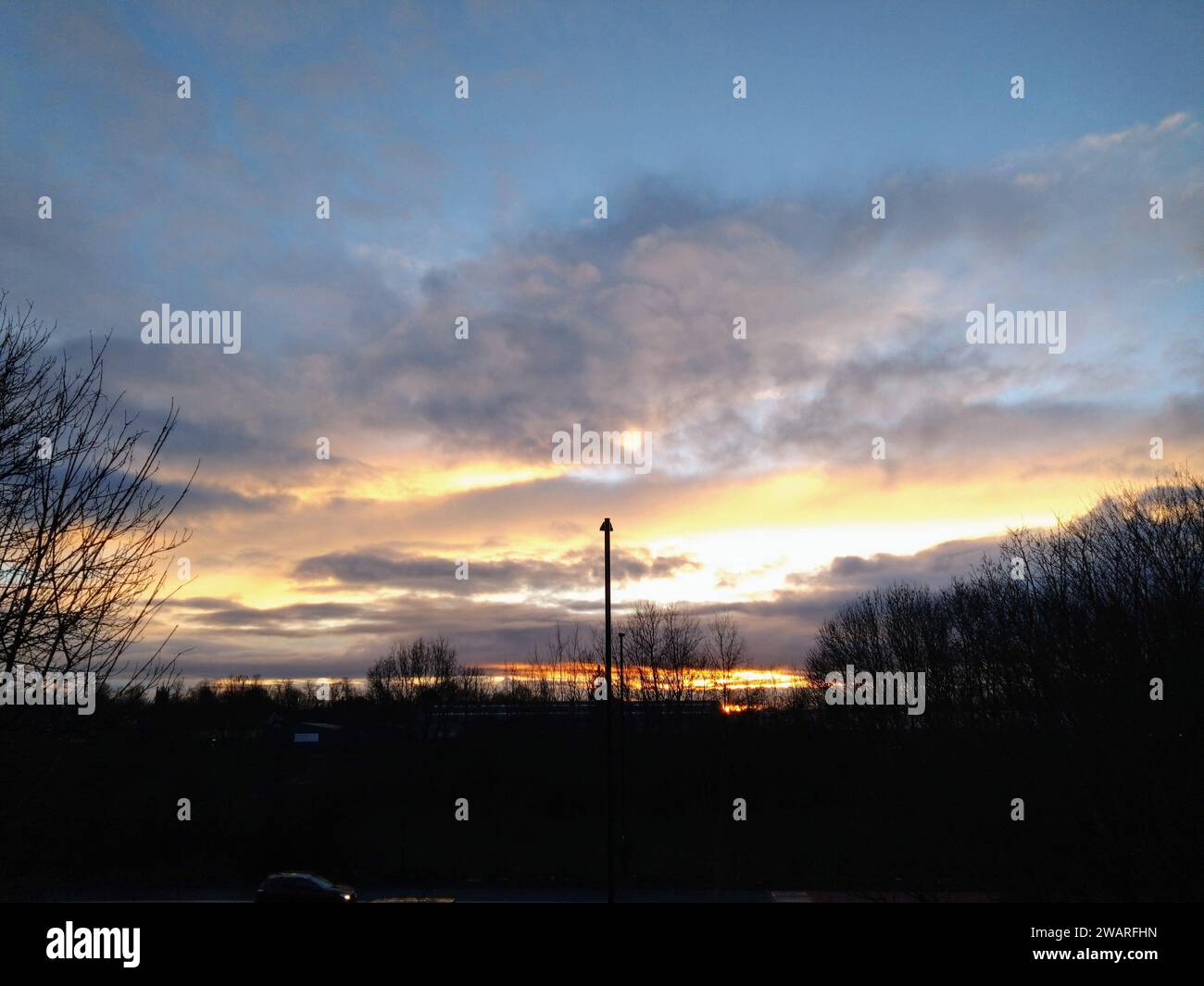 An evening sky featuring clouds, trees, a lamppost, and a car passing ...