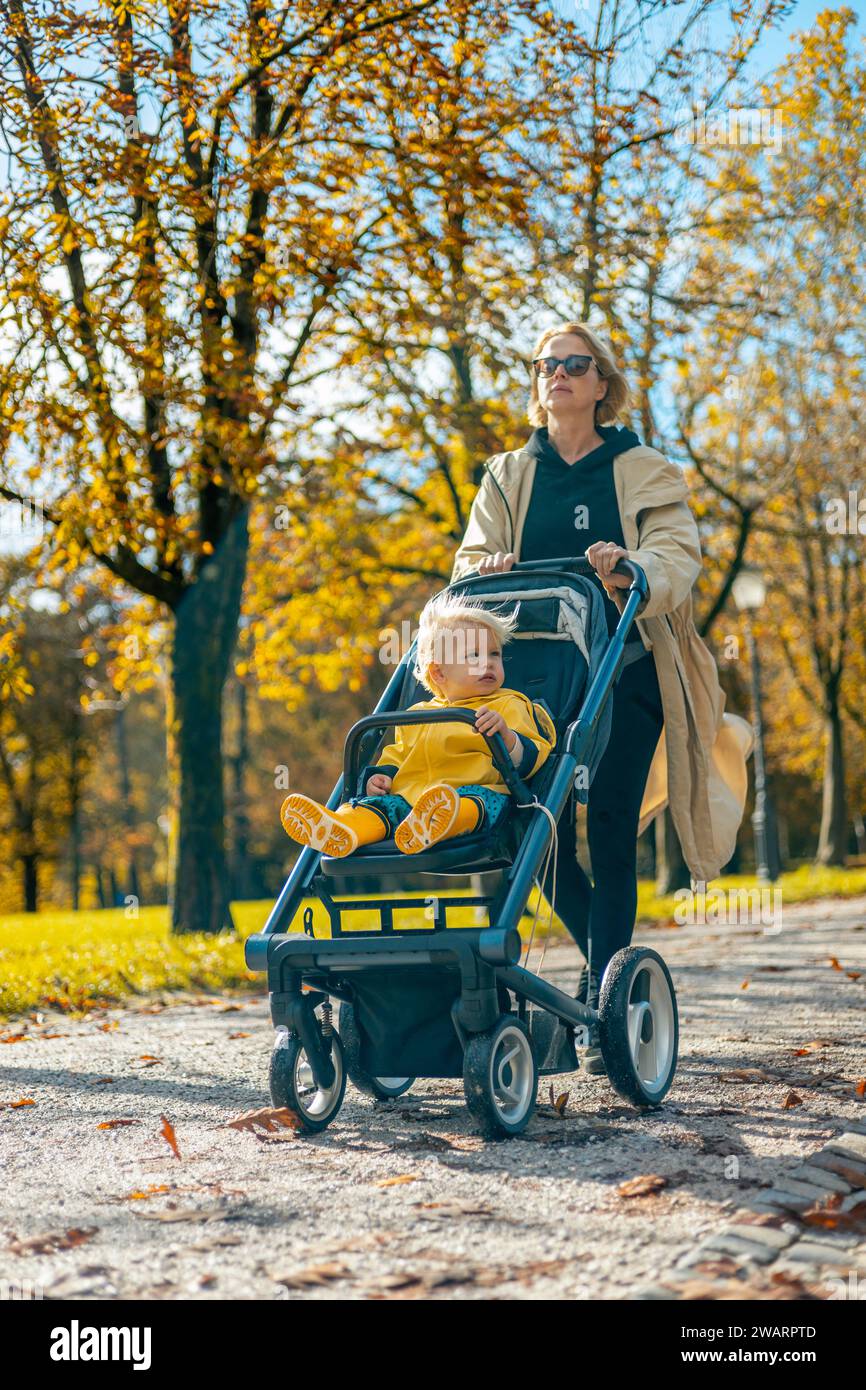 Young beautiful mother wearing a rain coat pushing stroller with her ...