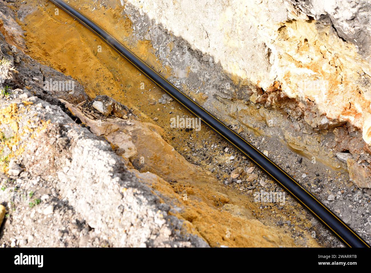 A plastic black gas pipe at the bottom of the trench. A dug trench for ...