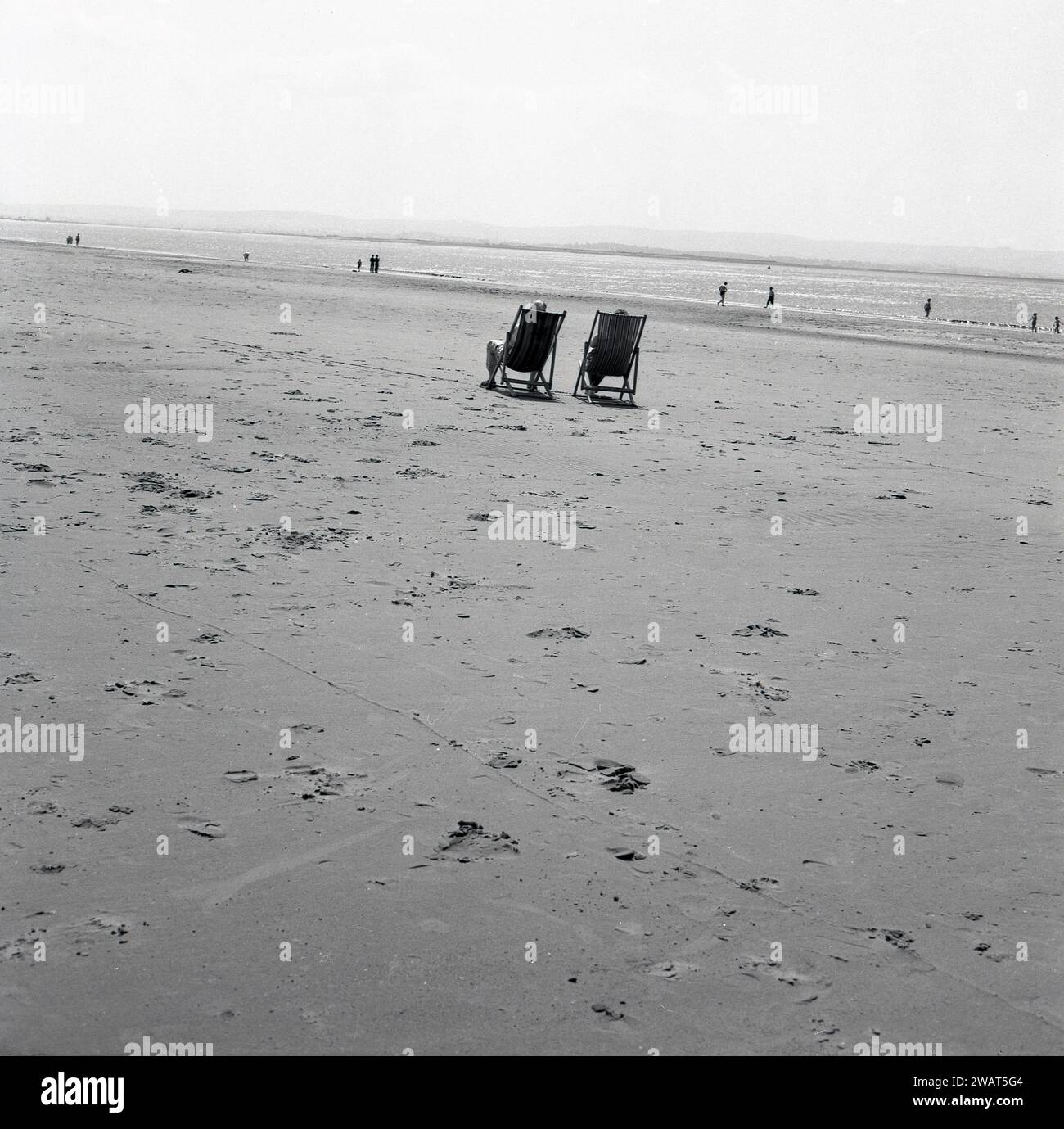 1960s, historical, on a wide empty beach, two people sitting on ...