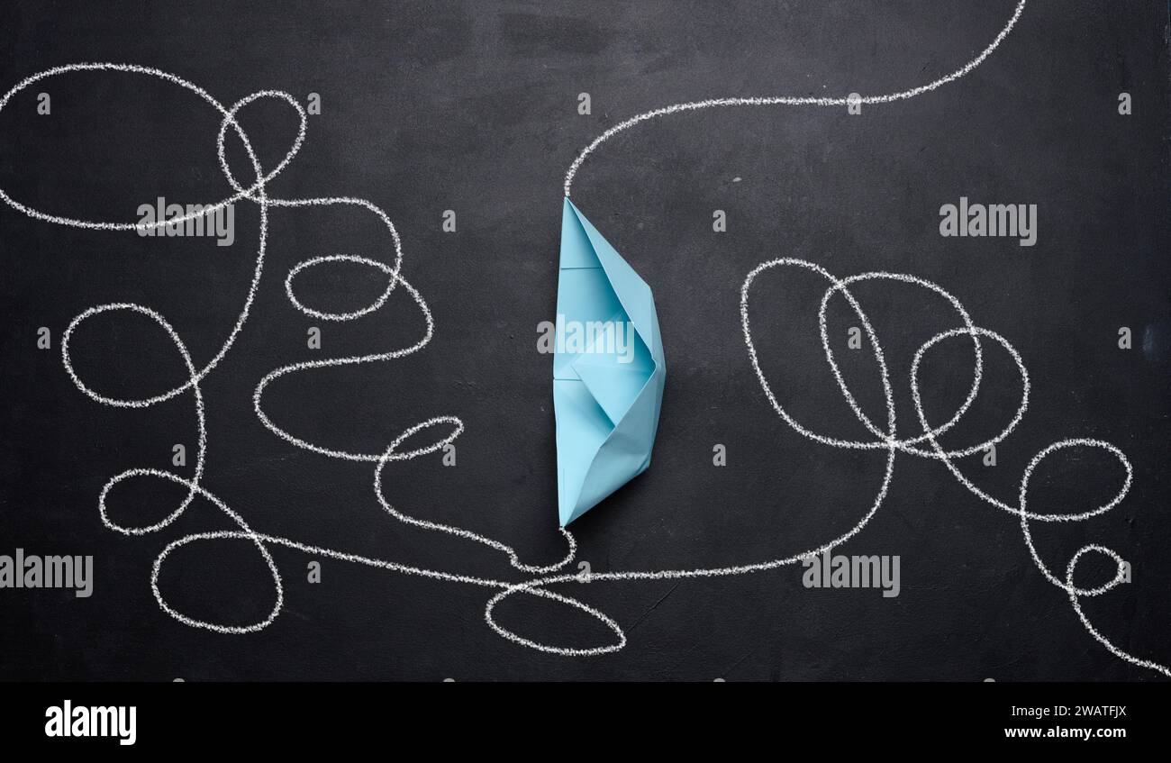 A blue paper boat and a tangled trajectory drawn in chalk. The concept ...