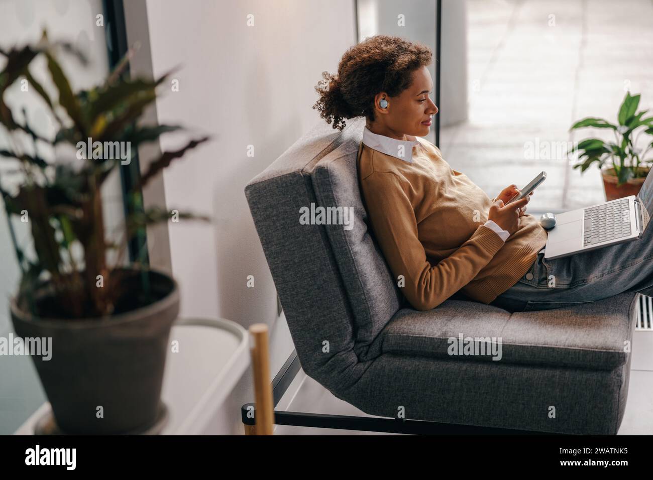 Stylish business woman is use phone while working on laptop in modern ...