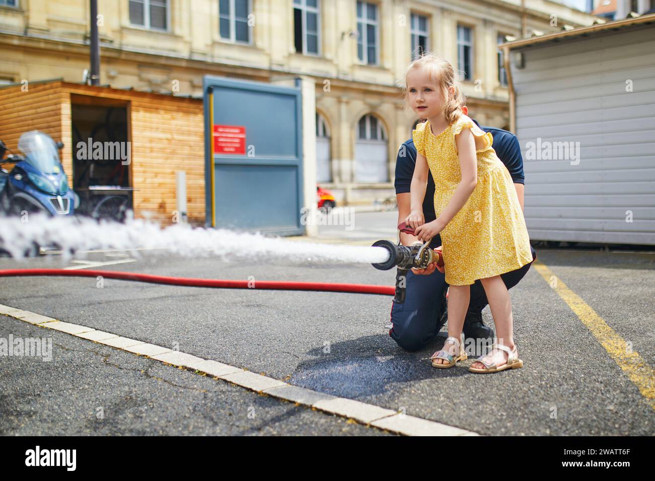 Adorable preschooler girl acting like a fireman holding firehose nozzle ...