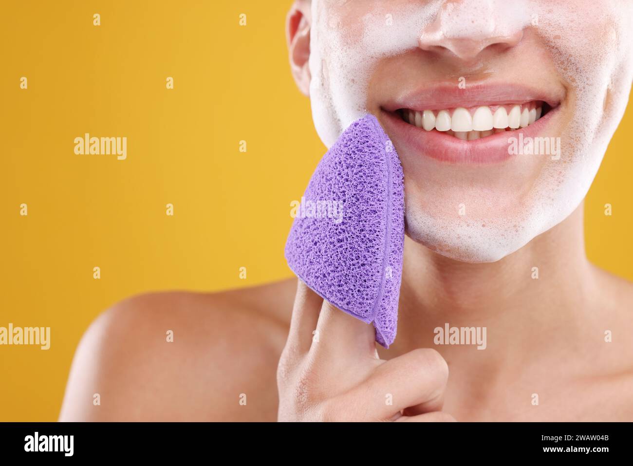 Happy young man washing his face with sponge on orange background ...