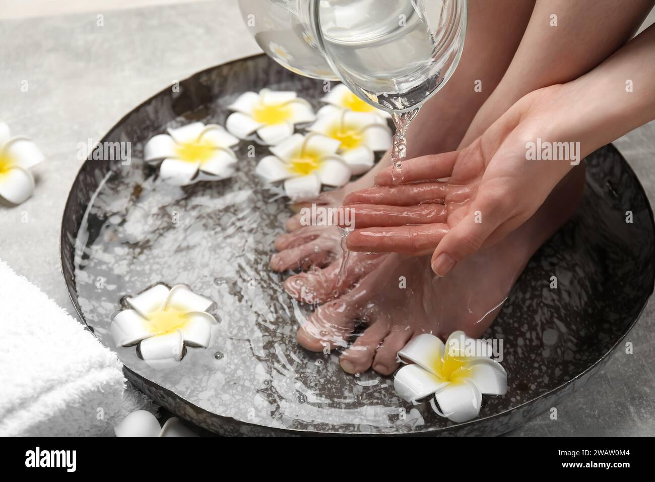 Woman pouring water onto hand while soaking her feet in bowl on light ...