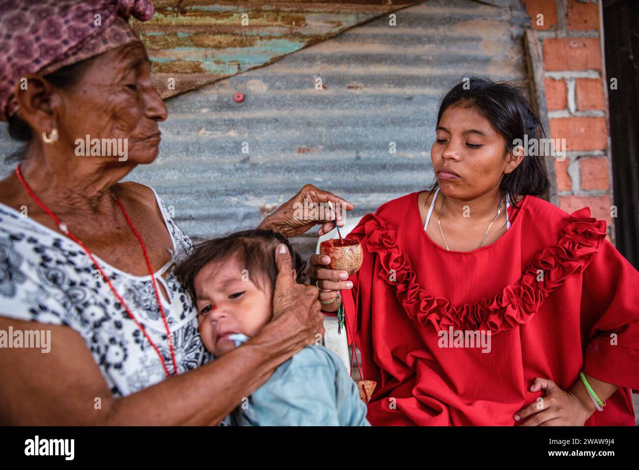 An elderly Wayuu woman face paints her grandchild before she takes part ...