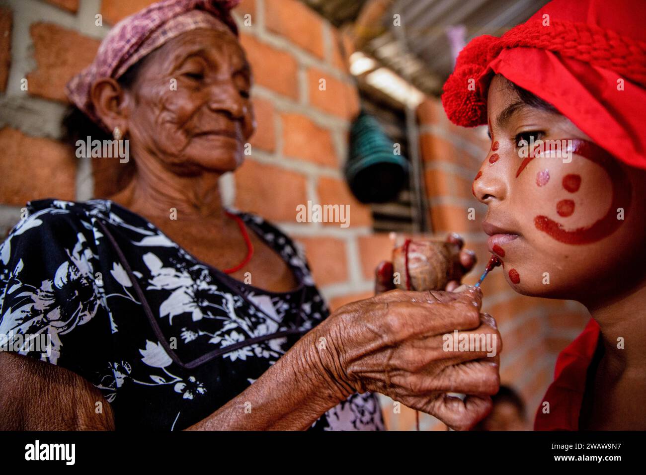 An elderly Wayuu woman face paints her grandchild before she takes part ...