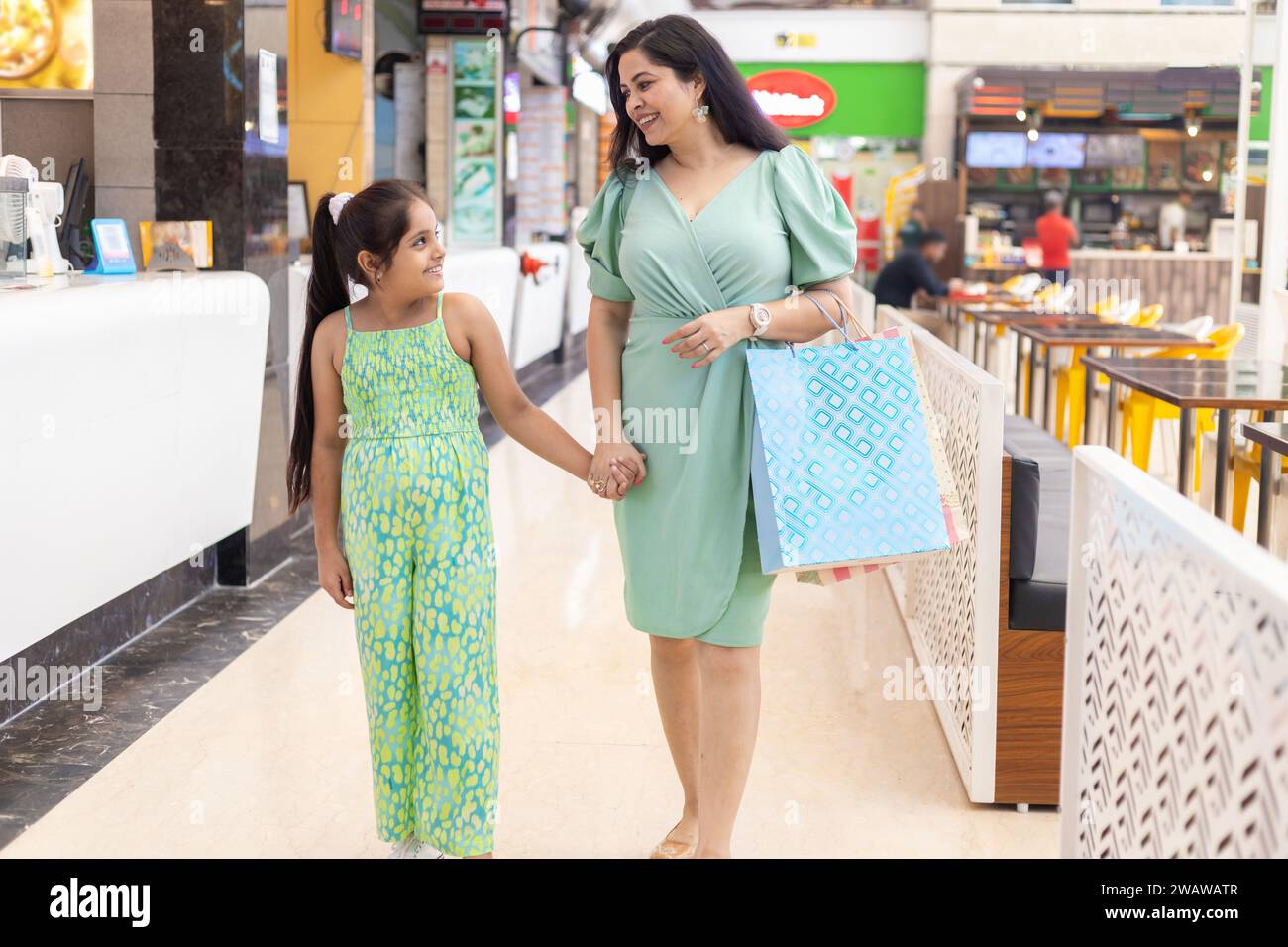 Happy Indian mother and daughter with paper bags, shopper bags walking in mall holding each ...