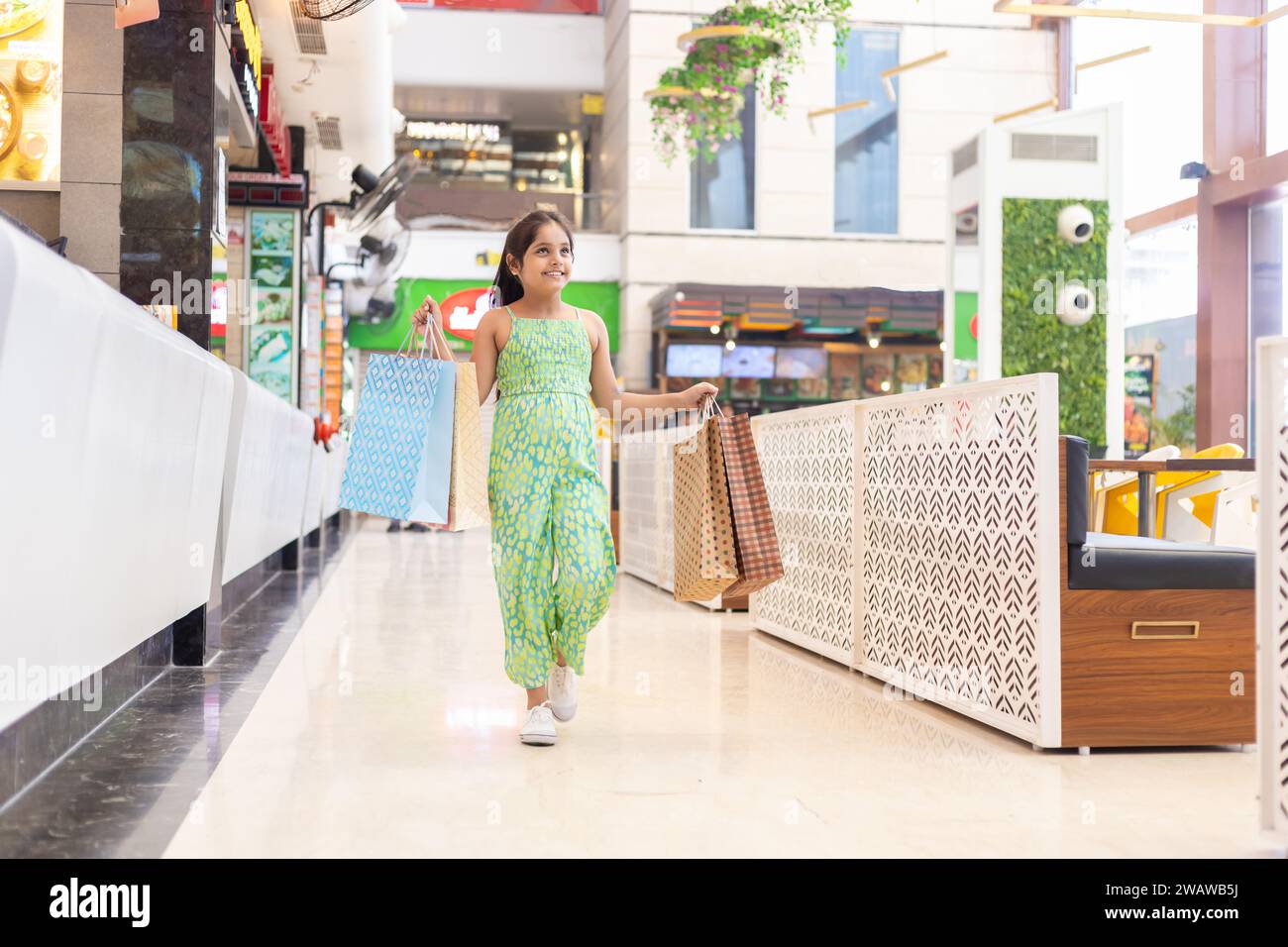 Happy Indian girl walking in shopping mall with paper bags, shopper bags in hands. Shopping ...