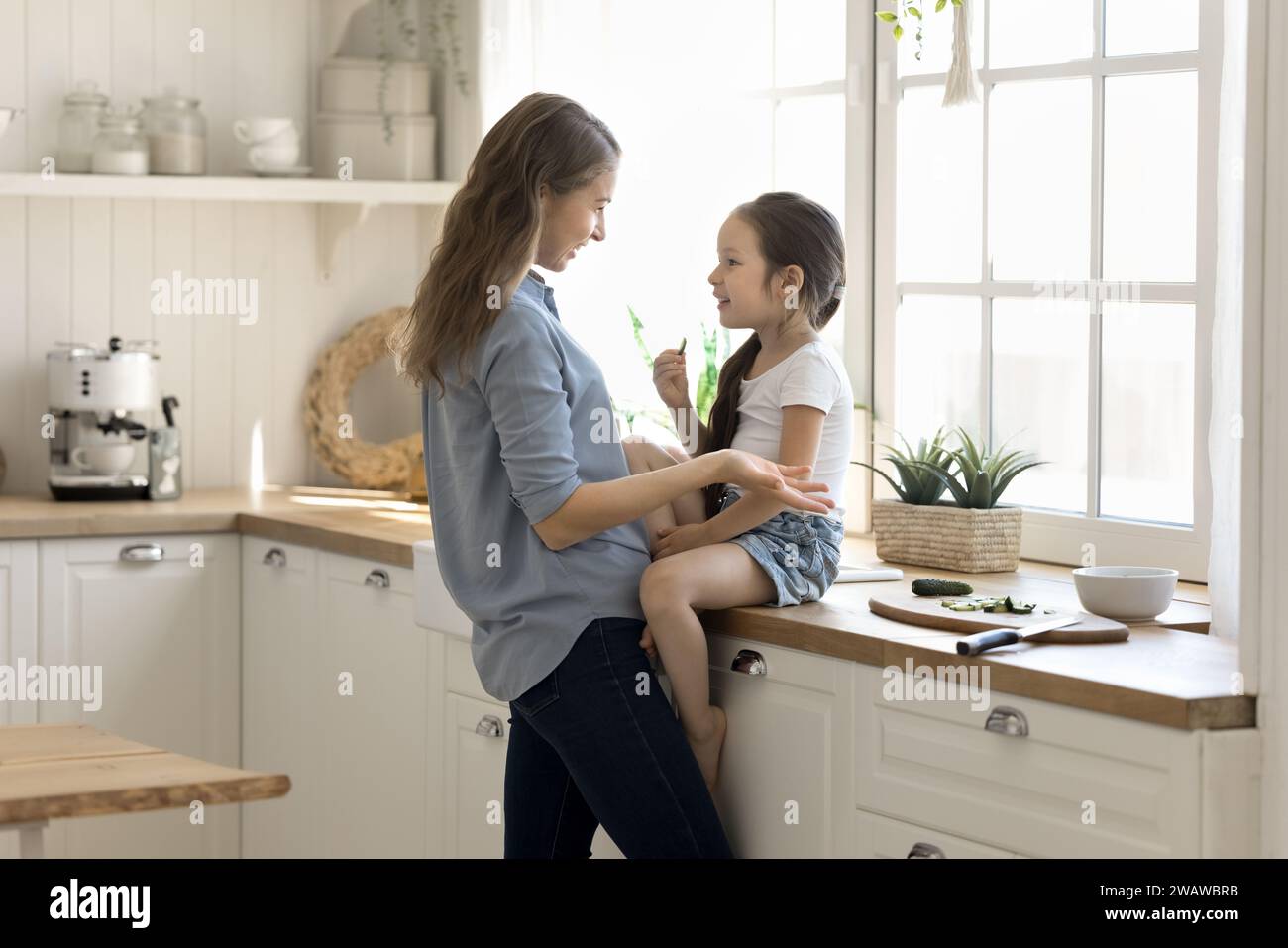 Girl sit on countertop talk to mother eating fresh vegetable Stock ...