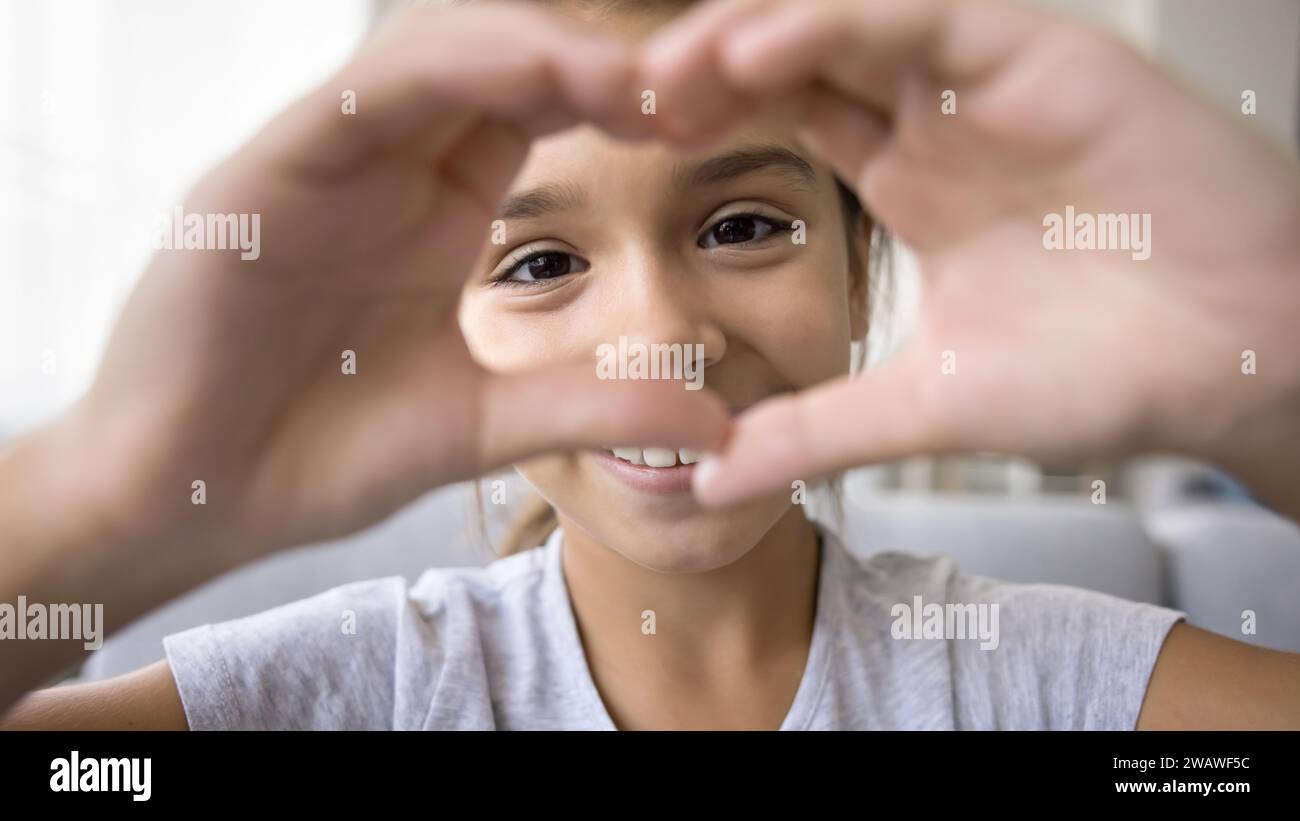 Happy school kid girl looking at camera through hand heart Stock Photo ...