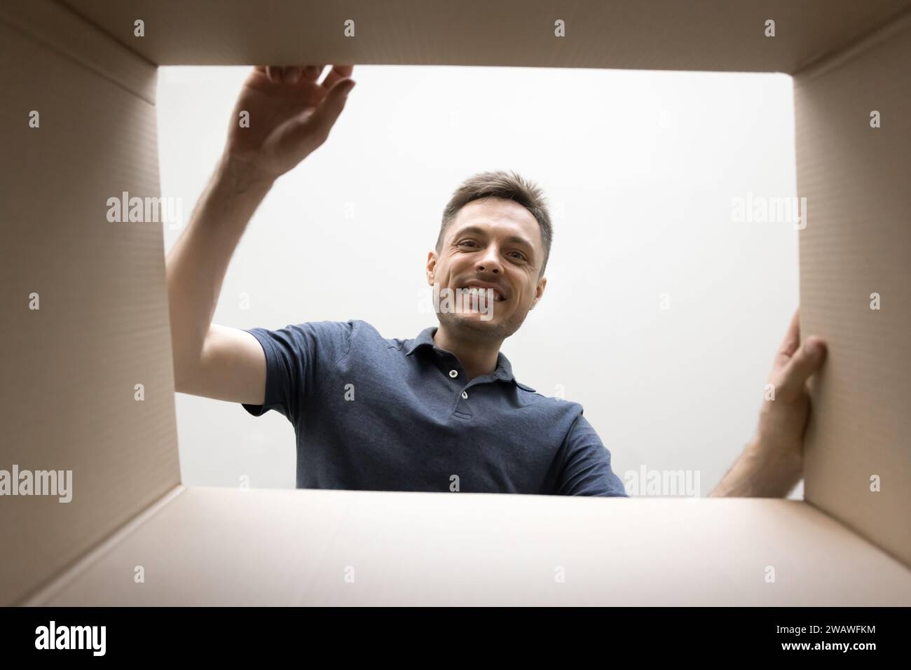 Positive young man opening large cardboard shipping box, looking inside ...