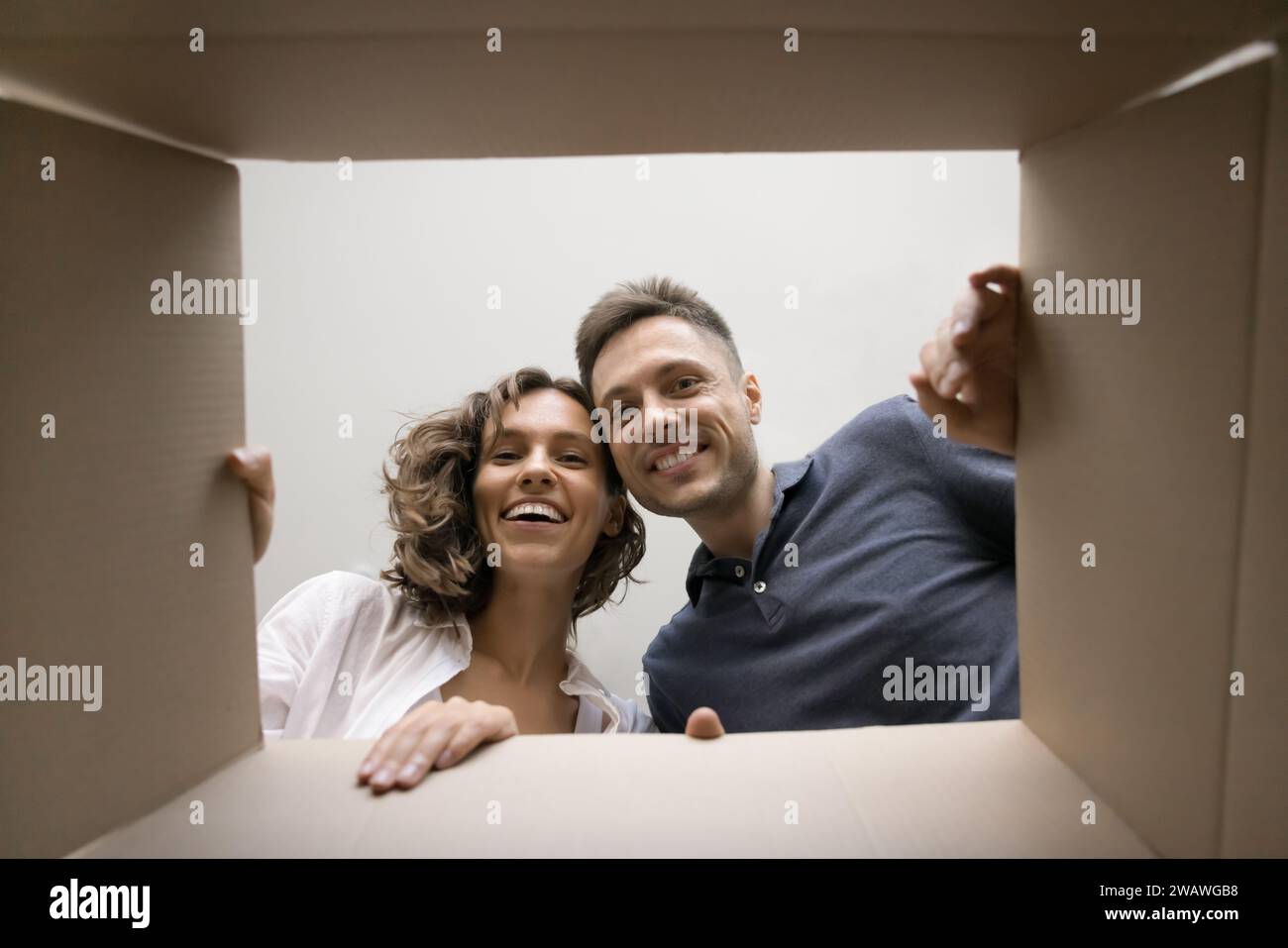 Cheerful young couple opening parcel, looking inside cardboard moving ...