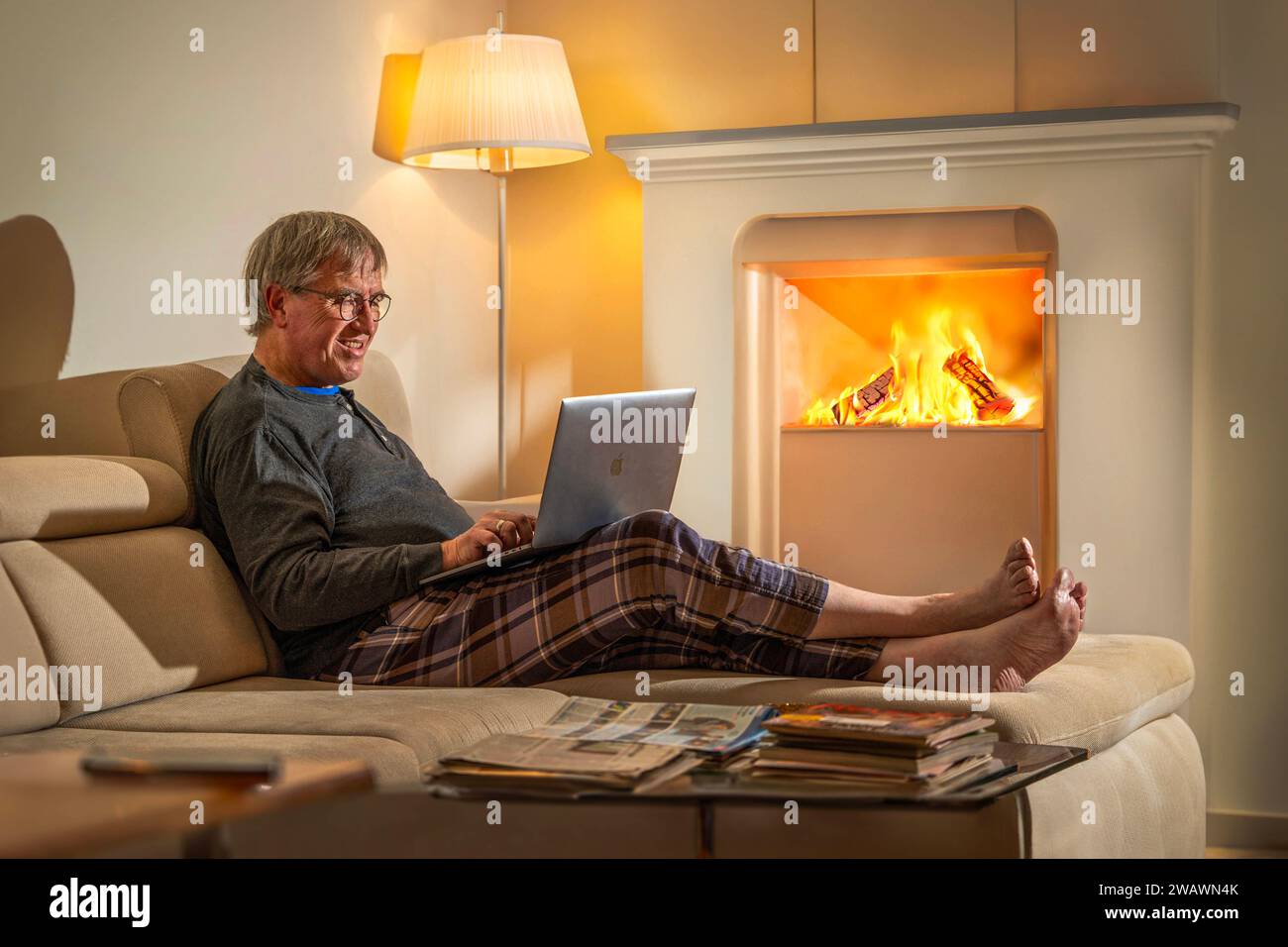 Mann sitzt abends allein zuhause gemütlich am Notebook, Kaminfeuer ...