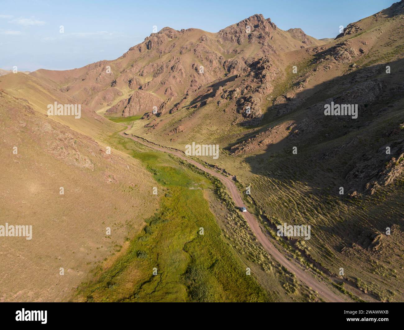 Aerial view, off-road vehicle on gravel road through a mountain valley ...