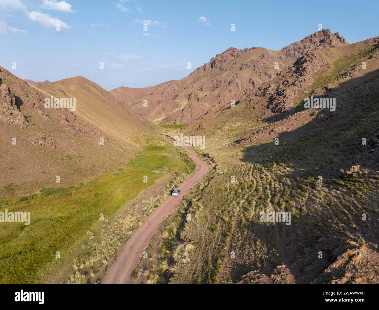 Aerial view, off-road vehicle on gravel road through a mountain valley ...