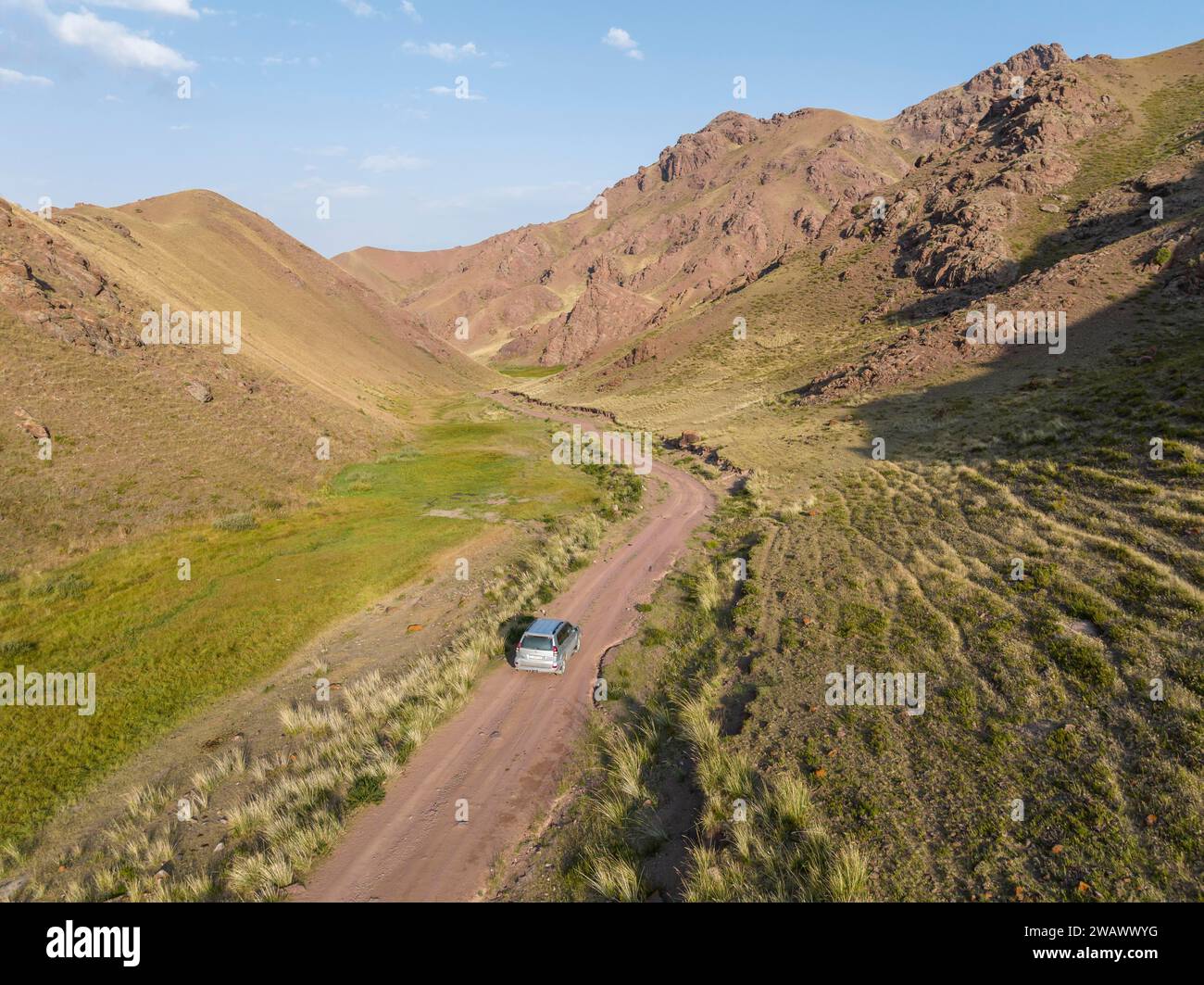 Aerial view, off-road vehicle on gravel road through a mountain valley ...