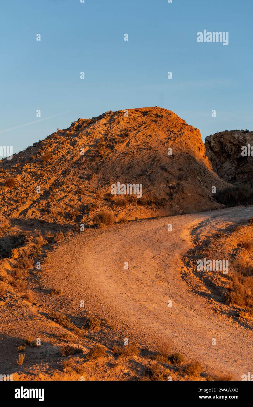 Dirt road in arid desert landscape with distant cliffs over sunset ...