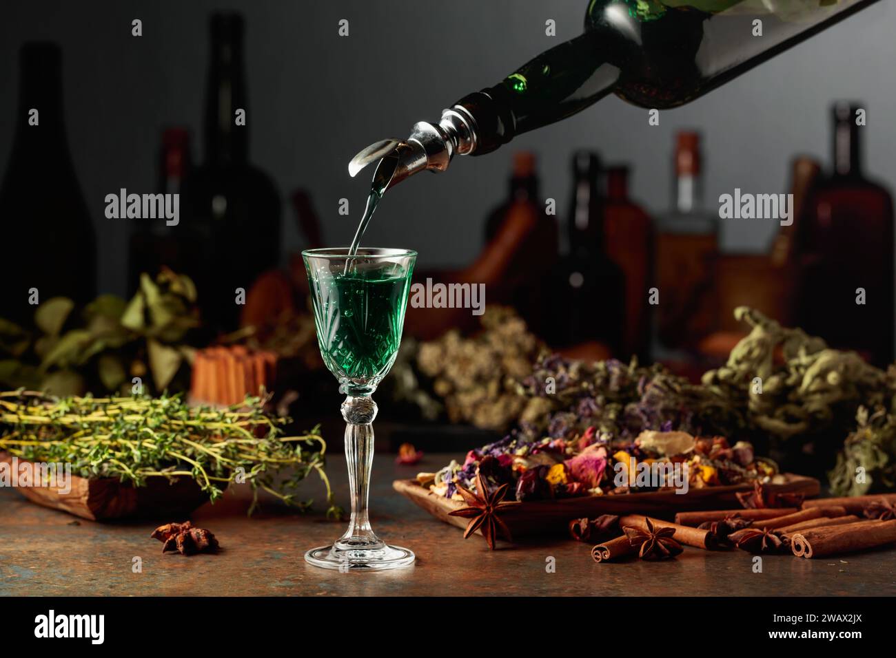 Green herbal liquor is poured from a vintage bottle into a glass. On a ...