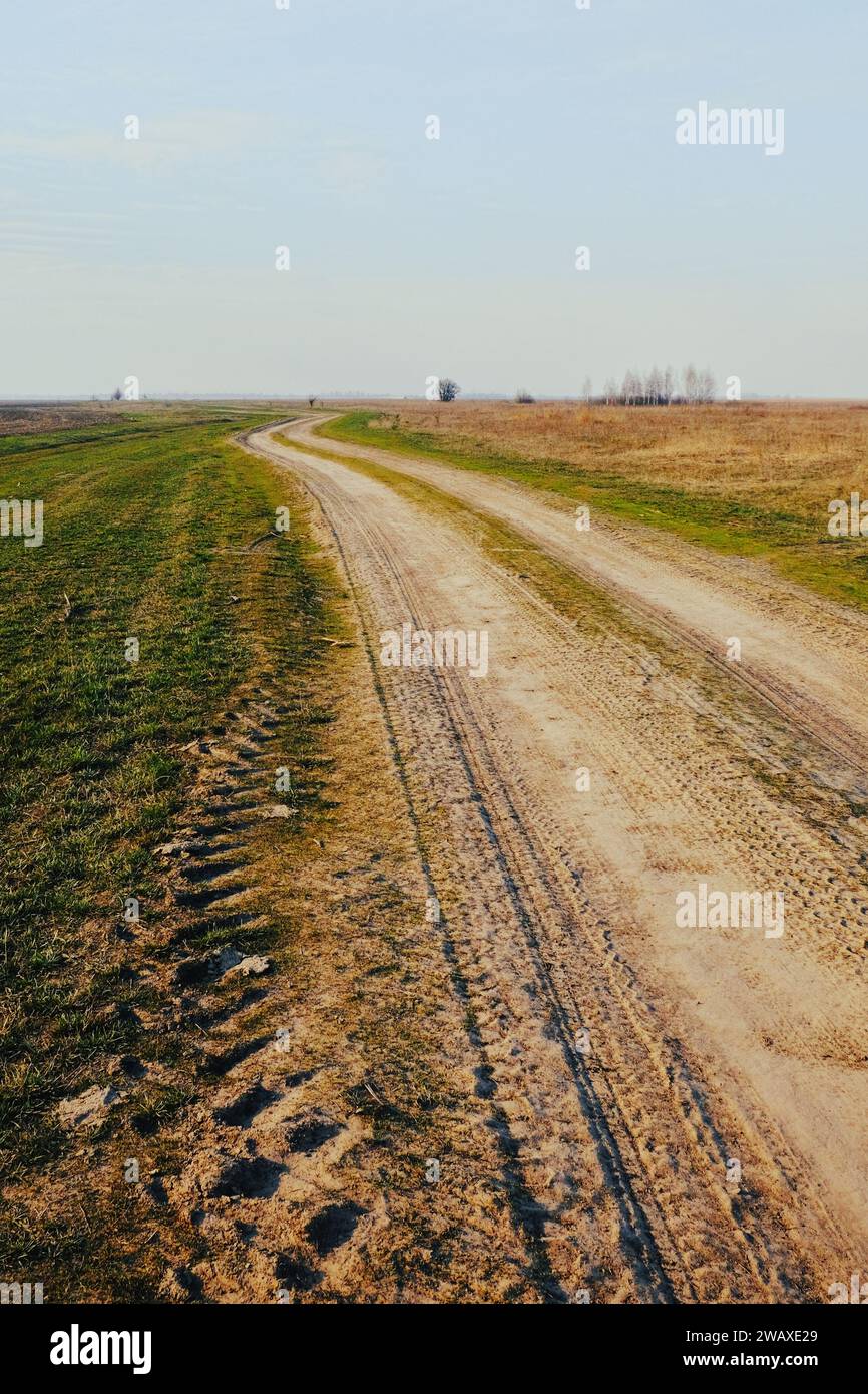 The image shows a winding path with tire tracks amidst an open field ...