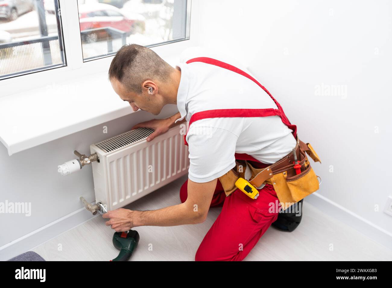 A male plumber installs a radiator in the heating system of an ...