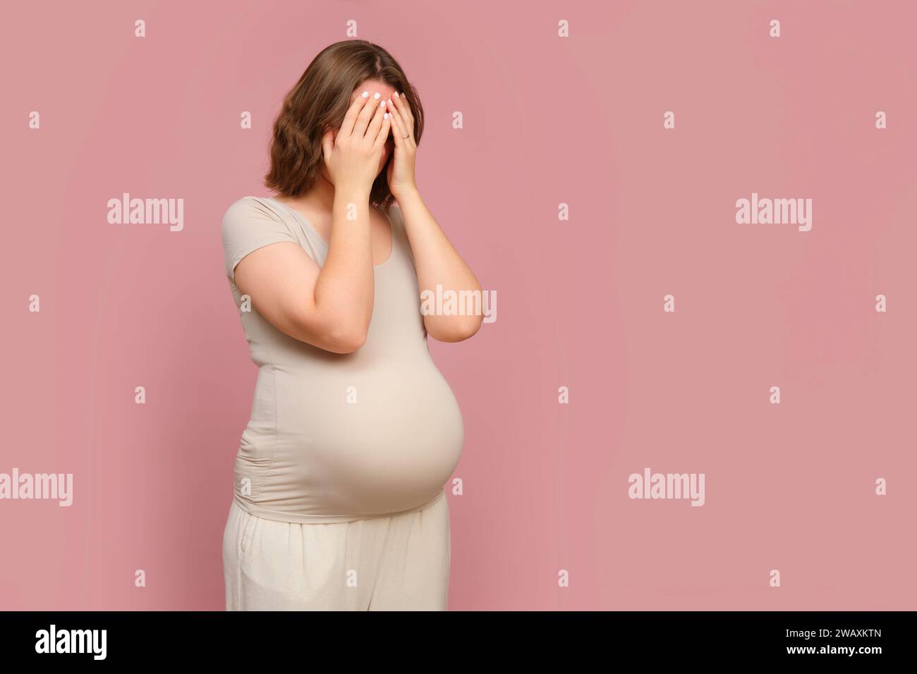A crying pregnant woman on a pink studio background. Pregnancy of an ...