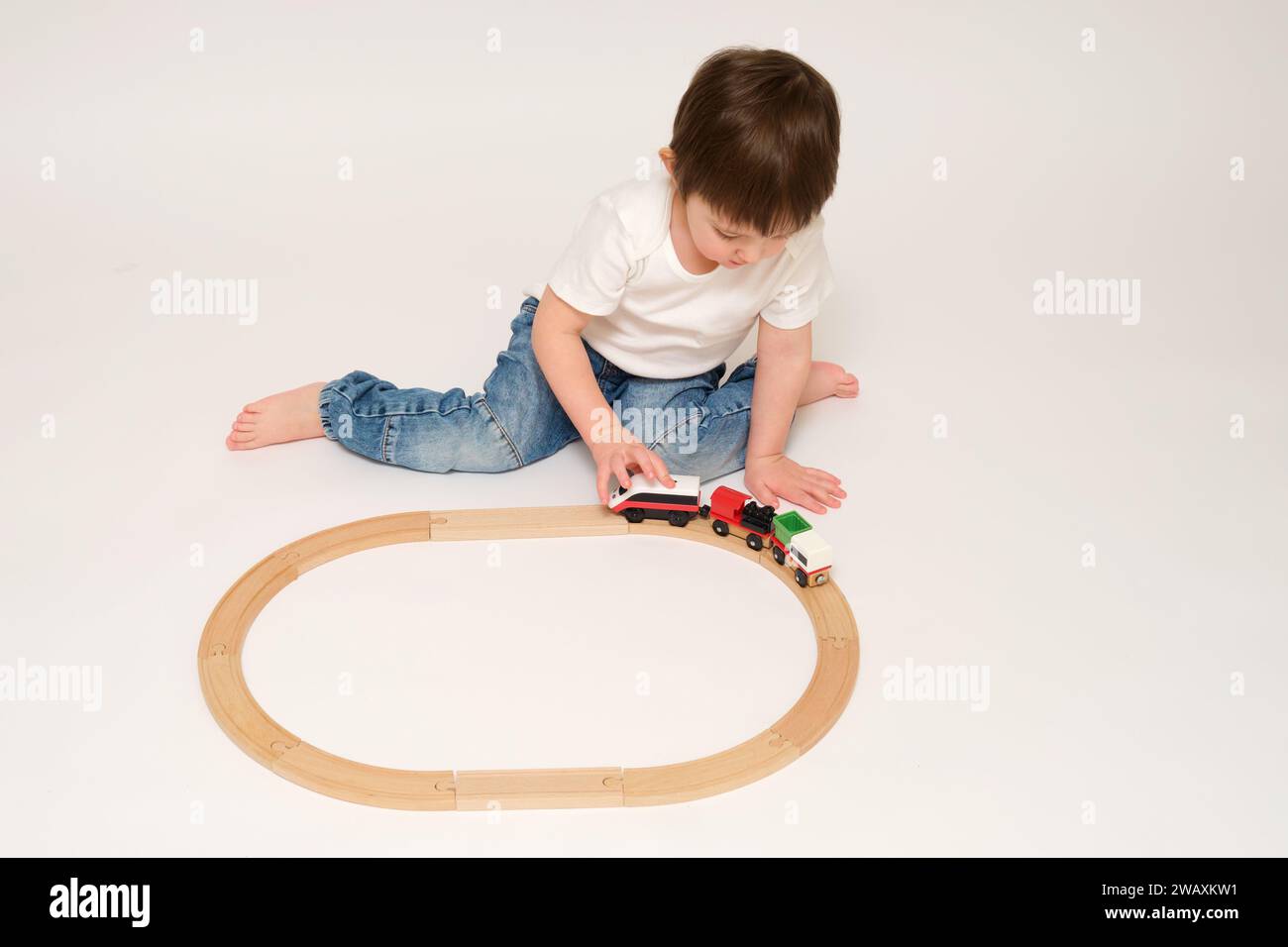 A child is playing train cars on the railway, studio white background. Baby with a toy train on ...