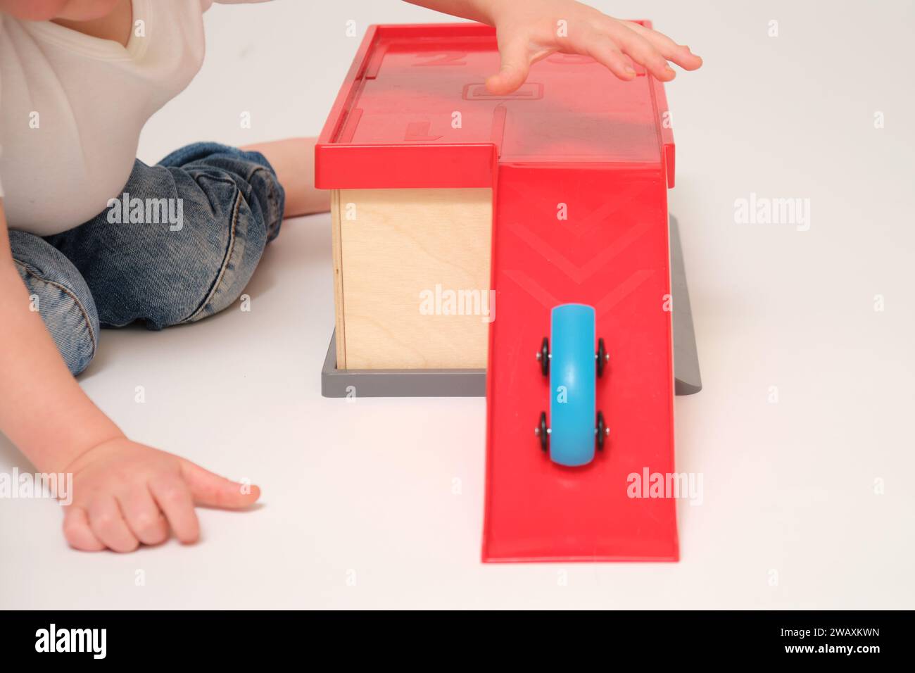 Toddler baby playing with cars in a toy garage, studio white background ...