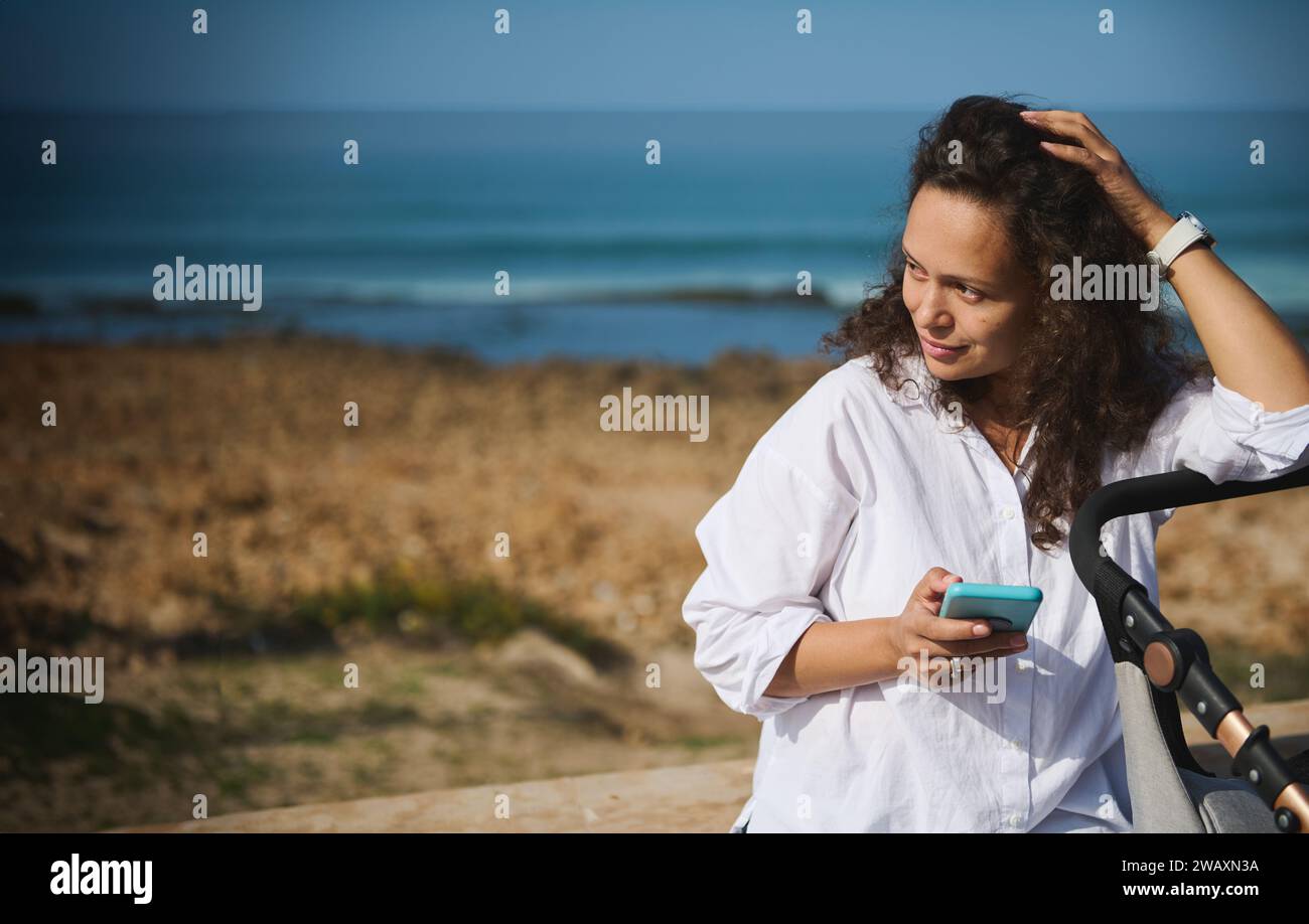 Beautiful woman mother pushing baby pram, checking her smart mobile ...