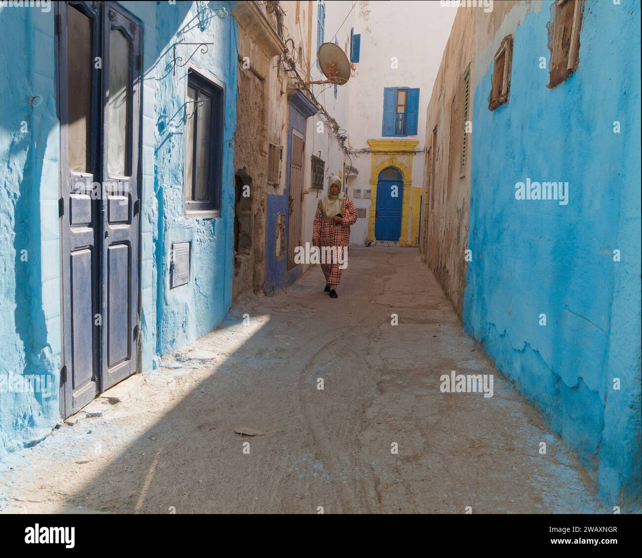 Lady walks down a narrow and colourful street with blue walls in the ...