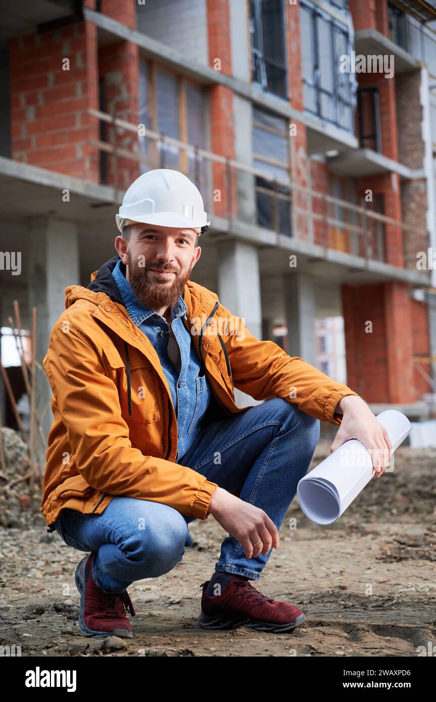Cheerful man in protective work helmet holding architectural building ...