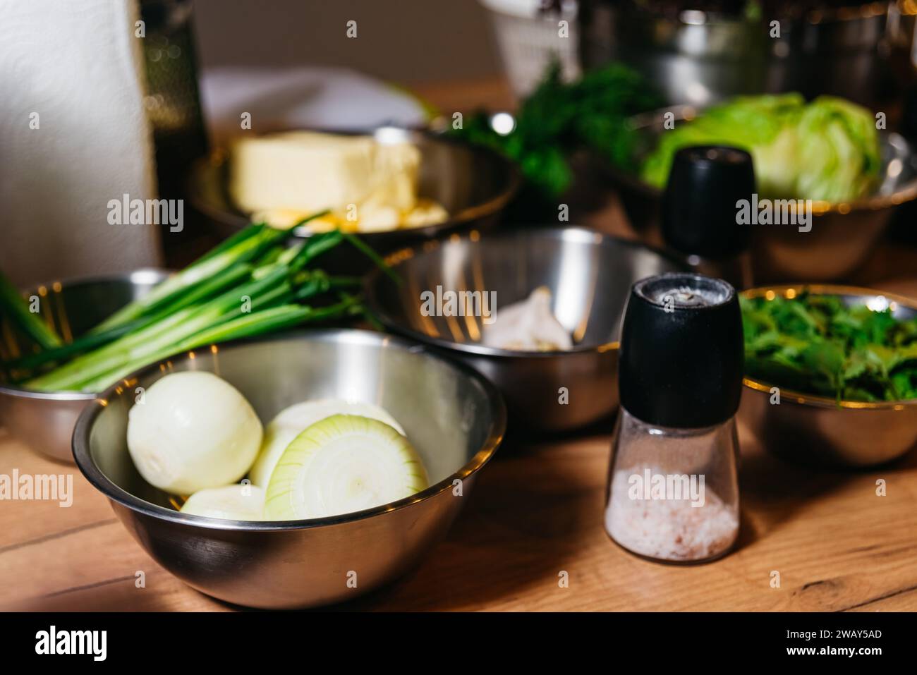 Cooking scene showcasing stainless steel bowls with onions and greens ...