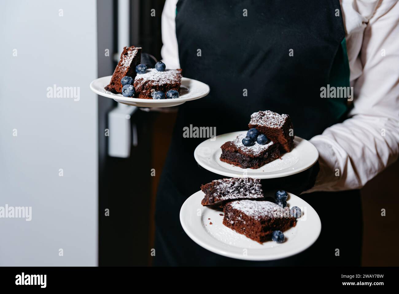 A waiter in a black apron presents two plates of rich chocolate cake ...