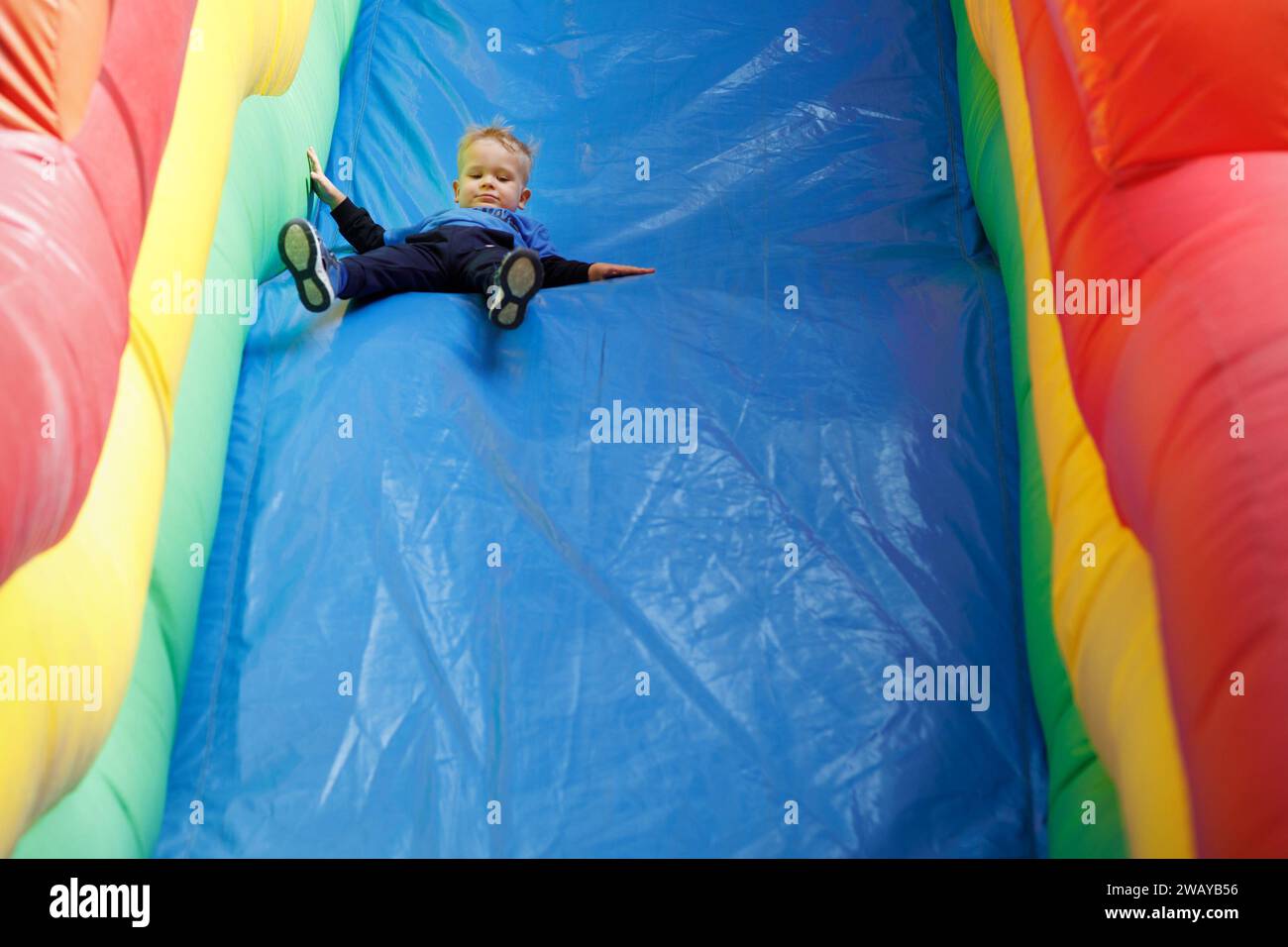 A little scared child sliding down an a blue inflatable slide. There is ...