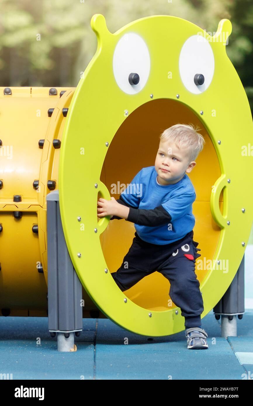 Cute boy going out from toy caterpillar mouth in public playground ...