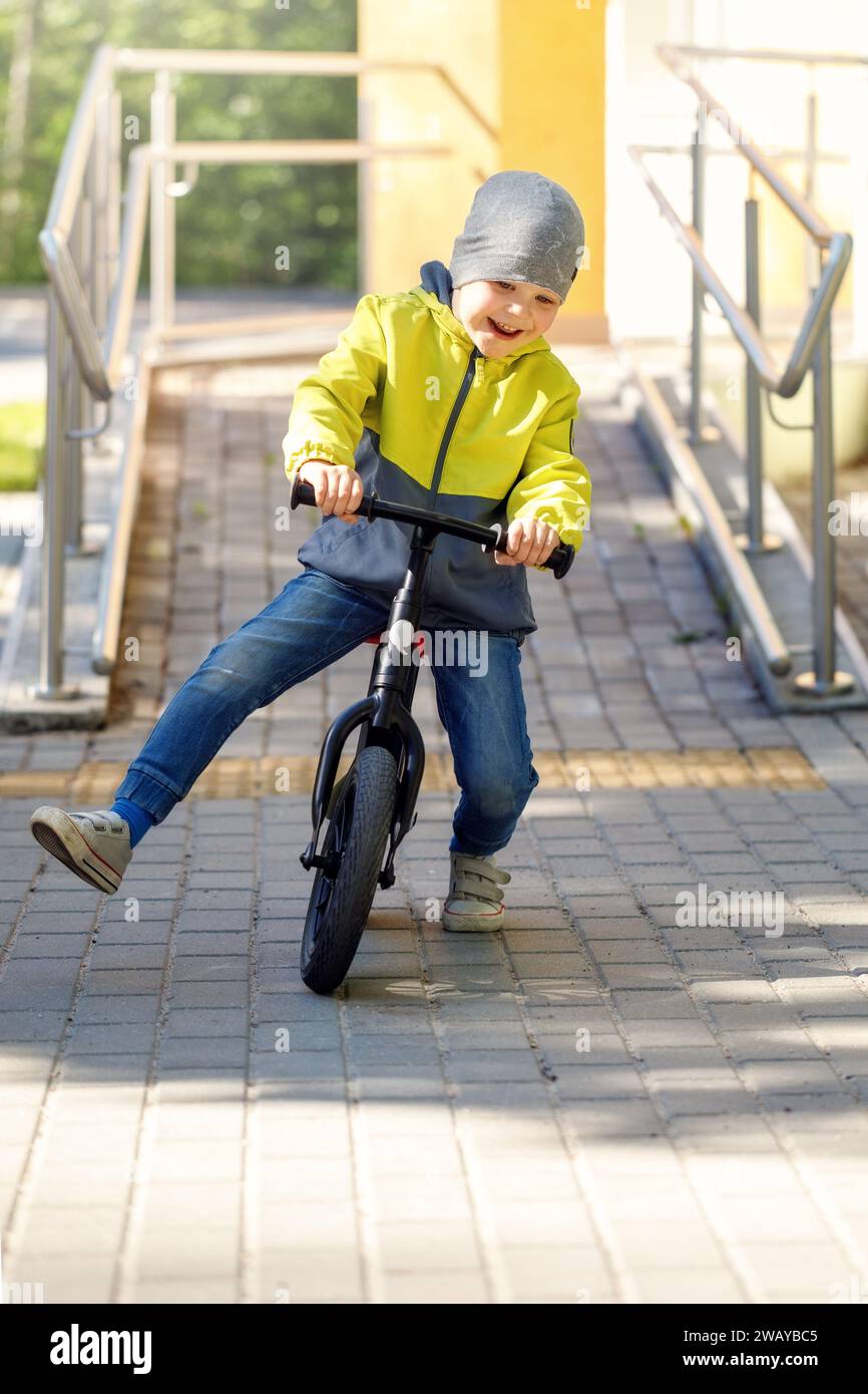 Happy cute boy wear yellow jacket and grey cap playing balance bike exercise in the morning day ...