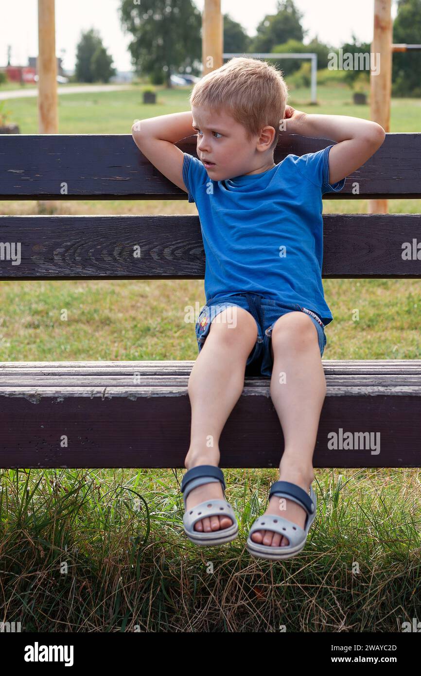 A sad lonely little boy sits on a buddy bench waiting for a friend to ...