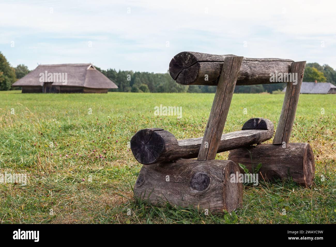 A wooden bench made of large logs stands in the wide green fields of ...