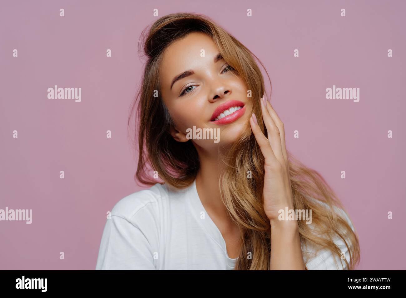 Confident woman with a gentle touch to her face, pink background Stock ...