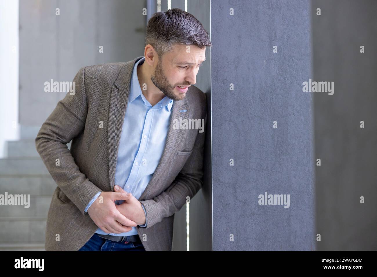 A sick young man businessman is standing in the office leaning against ...