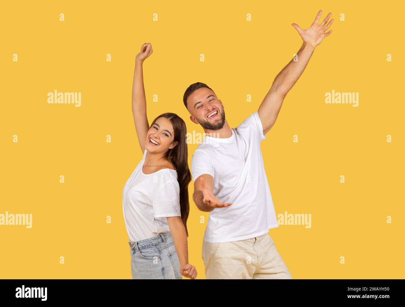 Joyful man and woman in white tops and denim joyously raise their arms ...