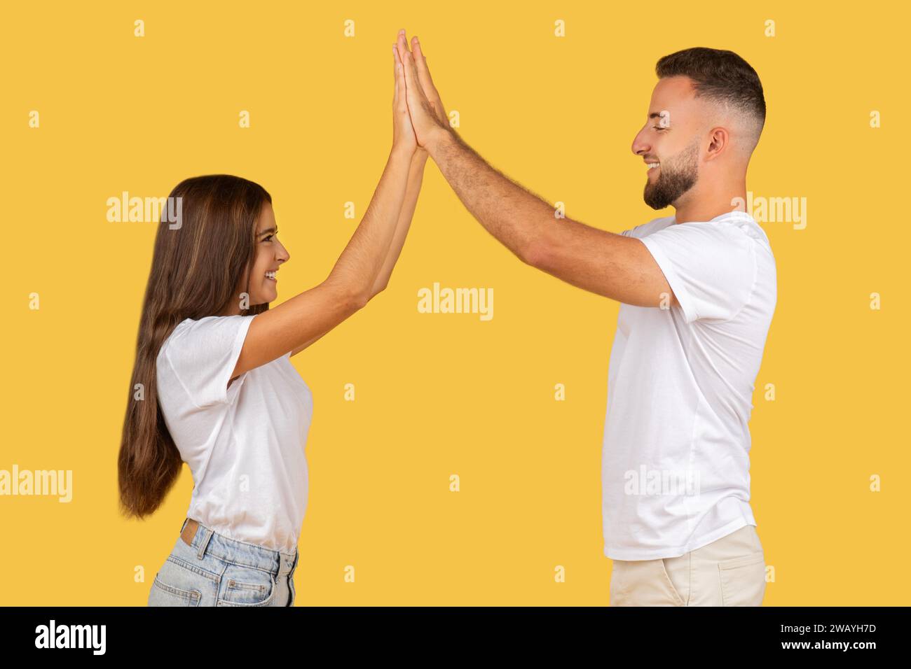 Energetic young couple in white t-shirts happily giving each other a ...