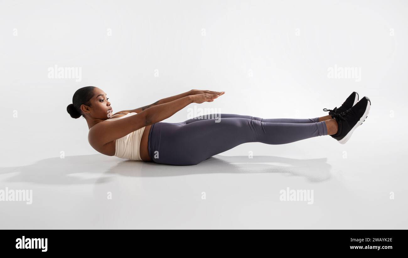 Determined young black woman performing V sit exercise, white ...