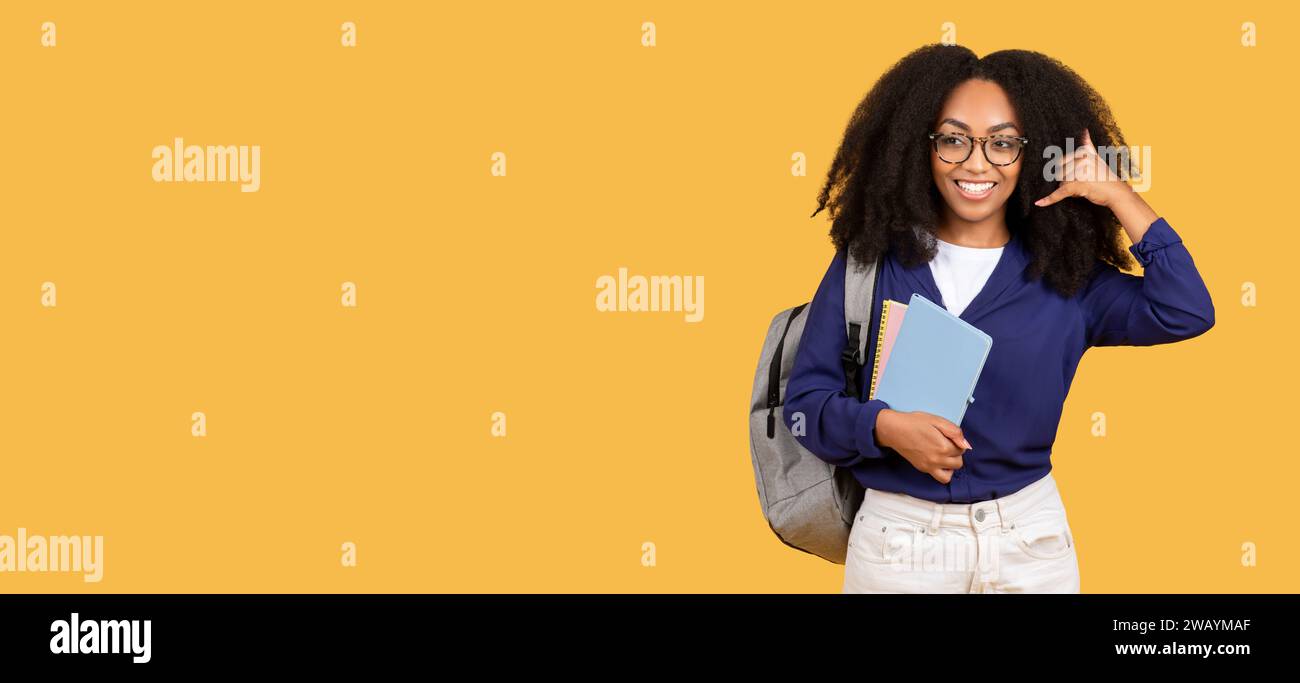 Happy black lady student with copybooks and backpack, making 'call me ...