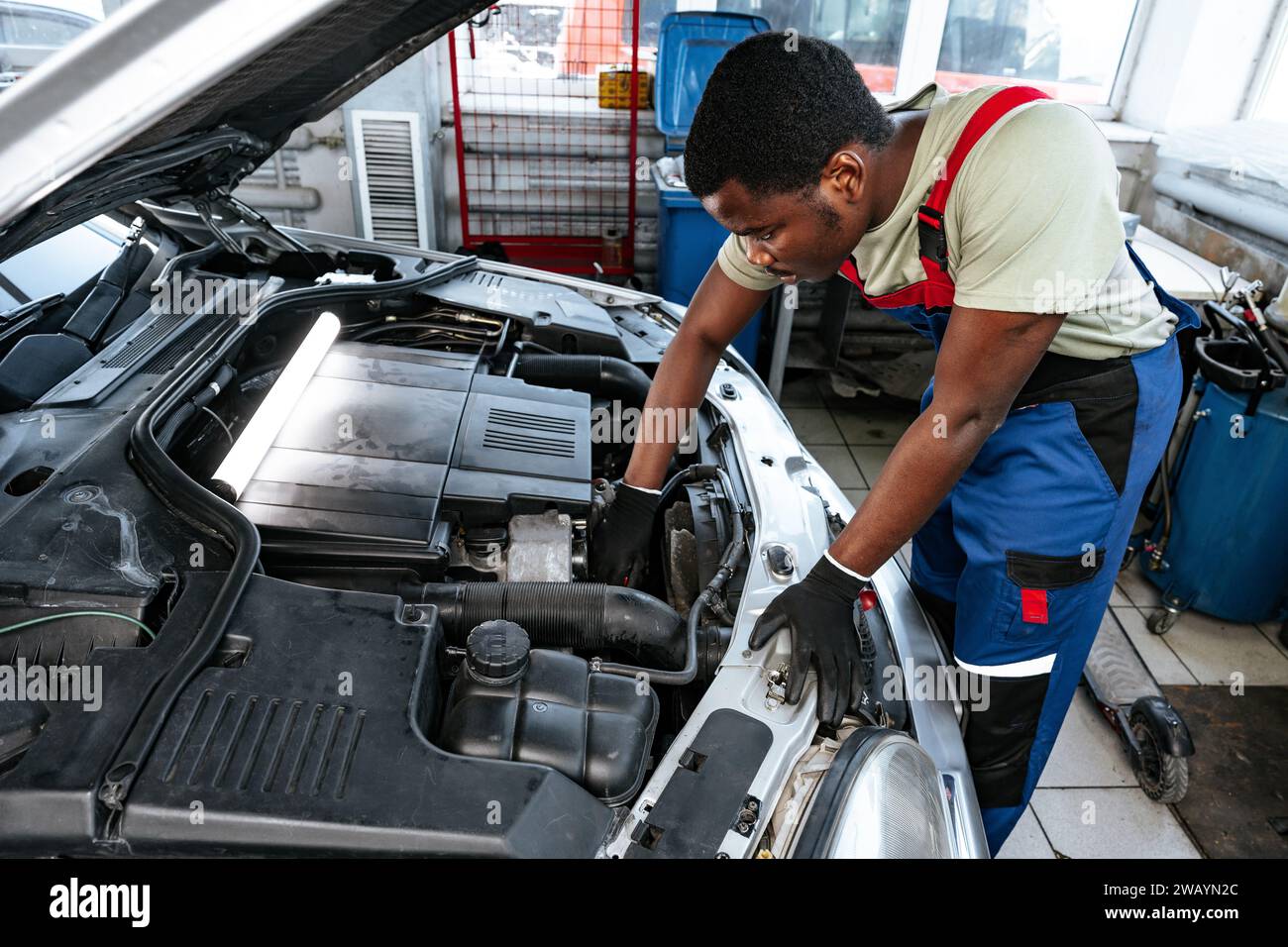 Young African man working under the hood of car fixing engine in auto ...