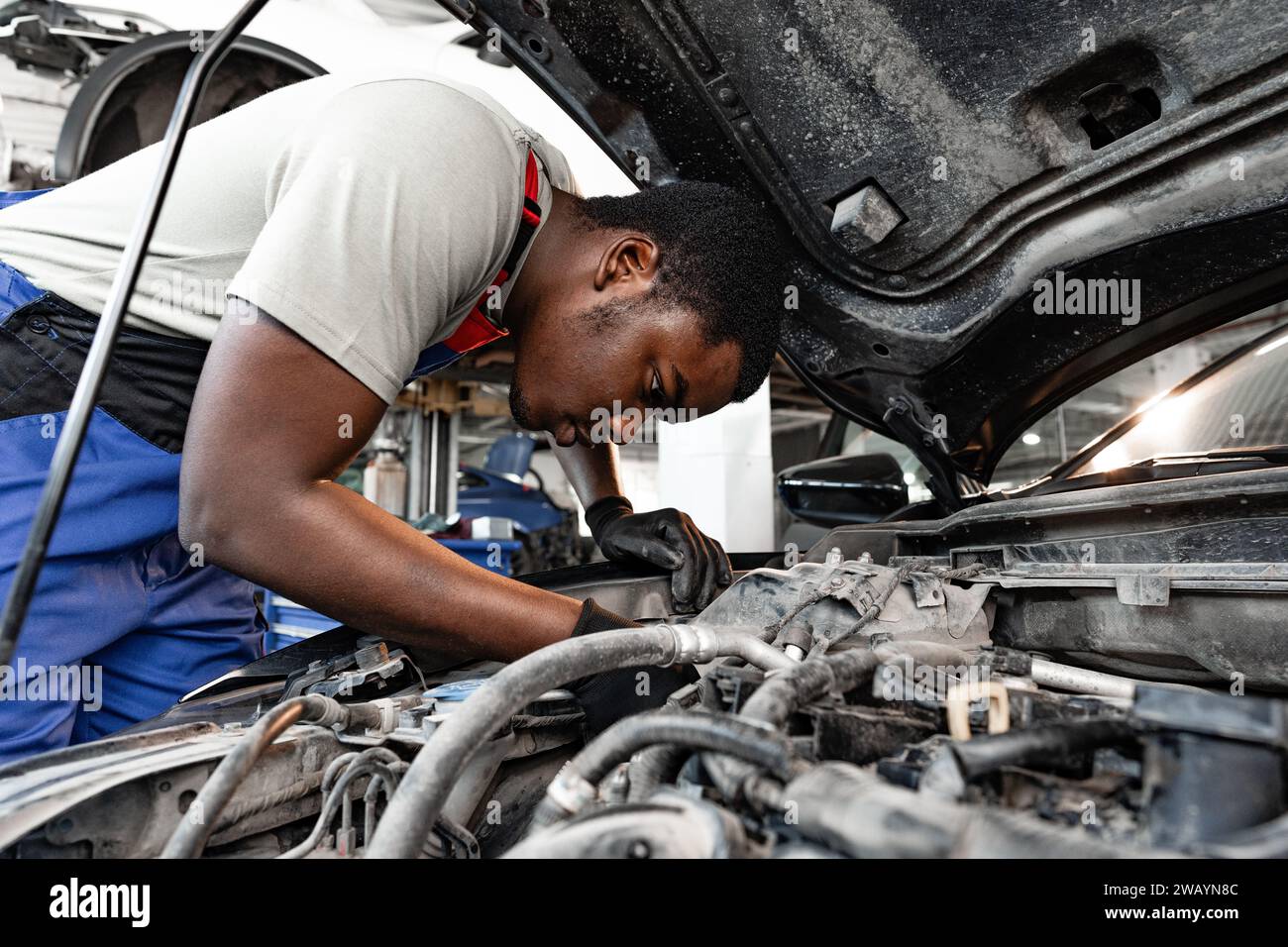 Young African auto mechanic checking car engine under the hood in auto ...