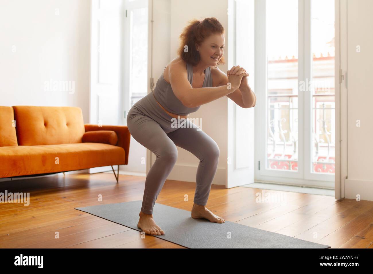 Smiling senior woman making squat exercise at home Stock Photo - Alamy