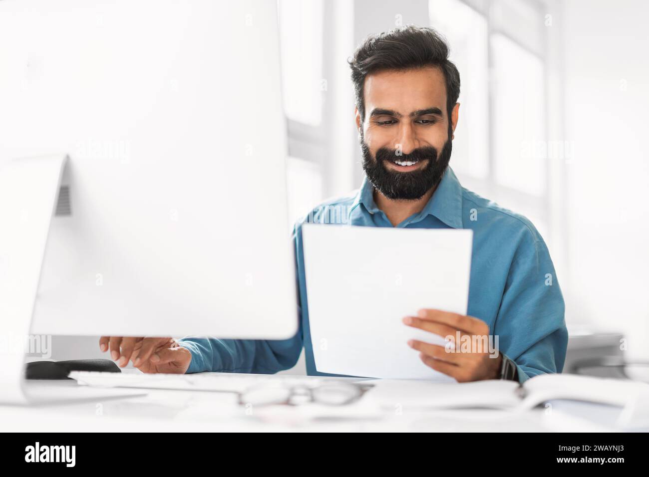 Content indian professional reviewing document at computer desk Stock ...