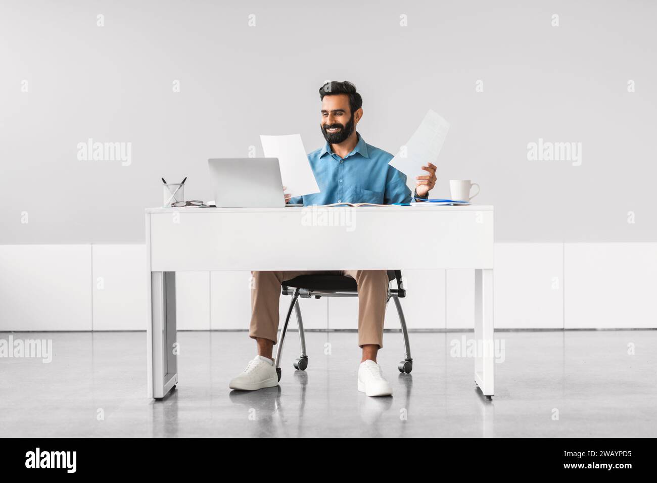 Happy indian professional man multitasking with documents and laptop ...